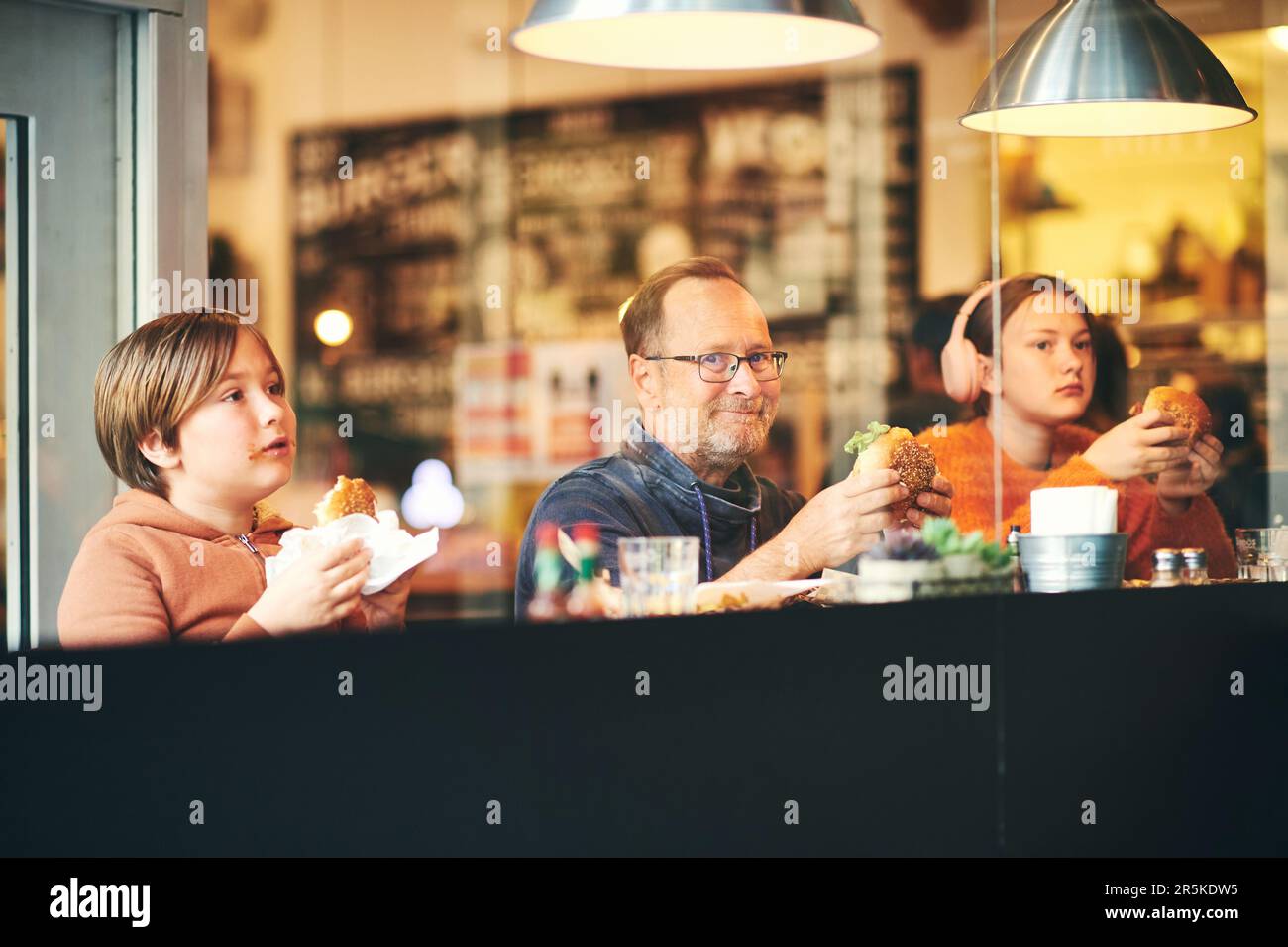 Family lunch, father with children eating hamburgers, in restaurant ...