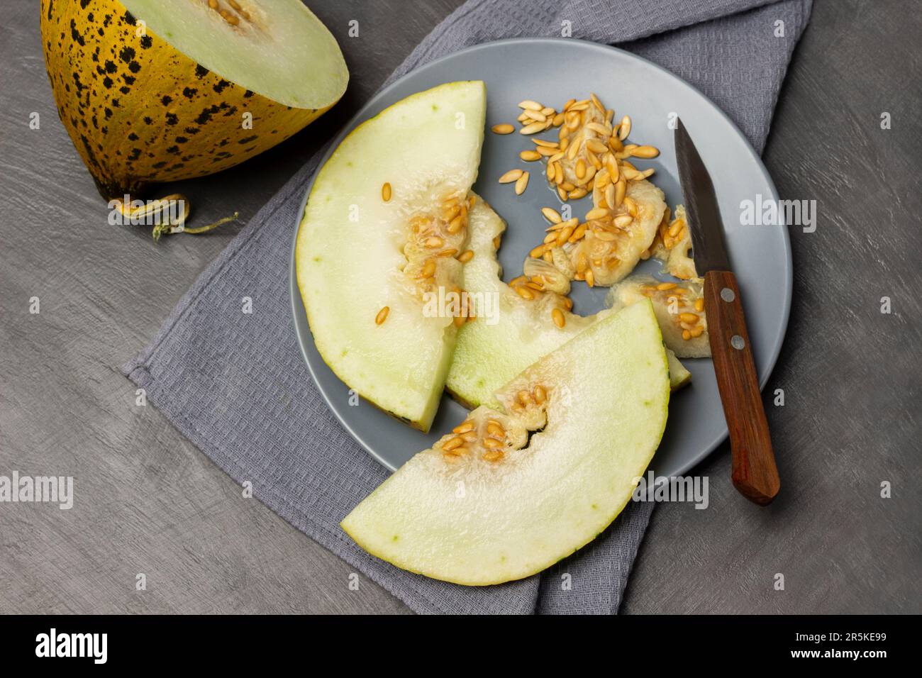 Half a melon. Melon slices with seeds and a knife on a gray plate. Gray ...
