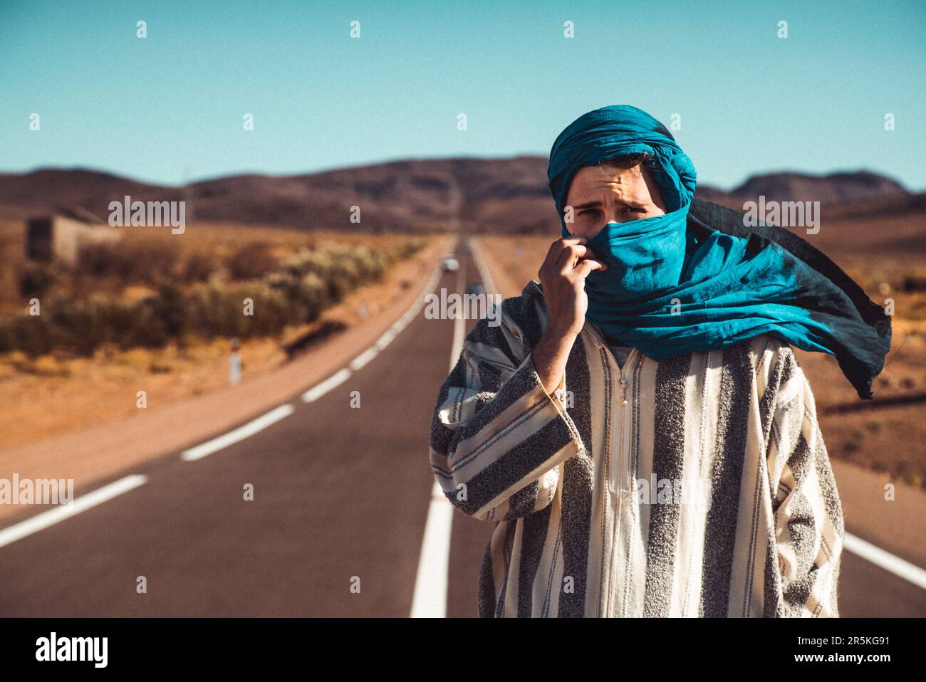 Portrait of a young white man dress as berber in the desert, blue scarf ...