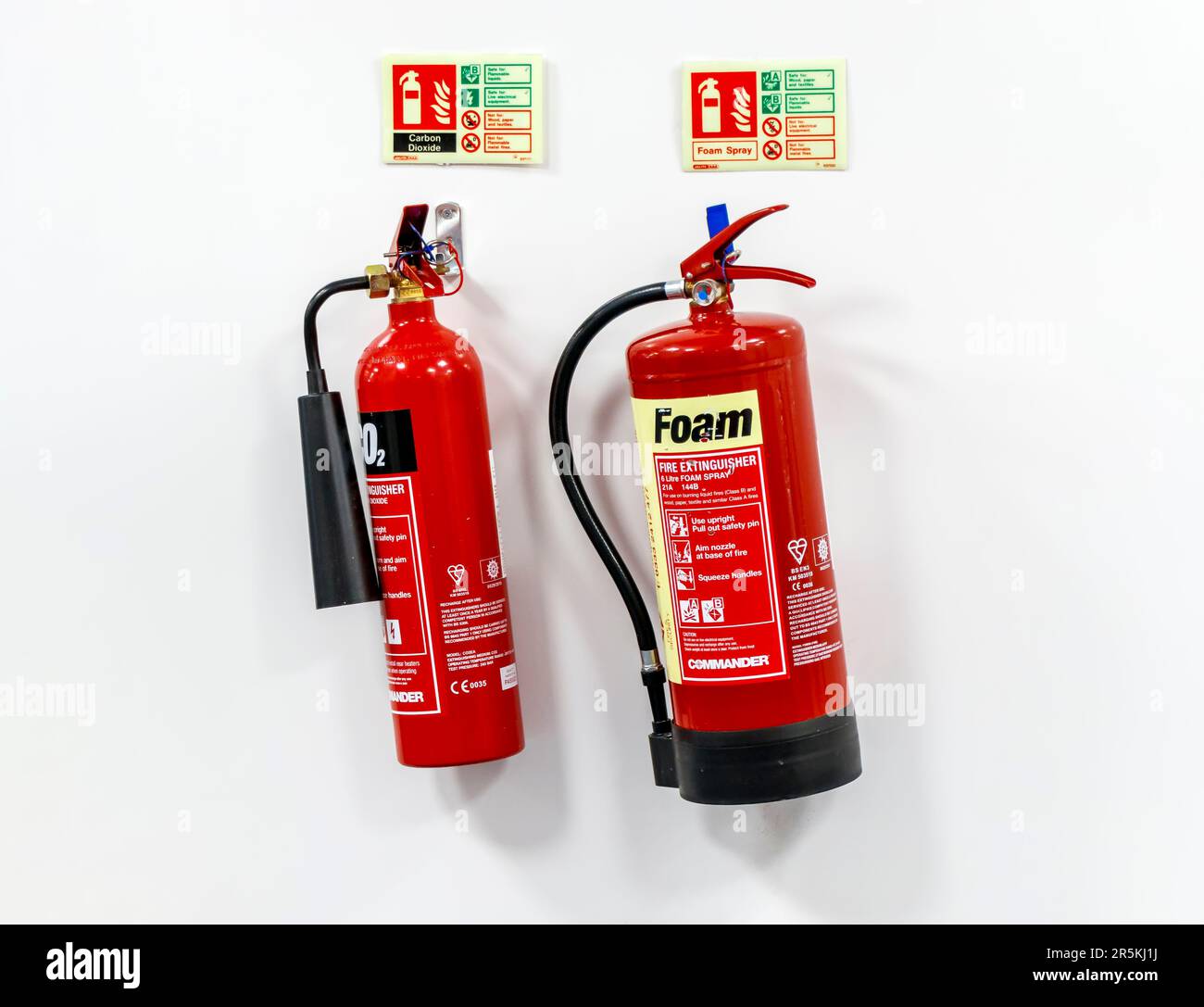 Two red fire extinguishers, one foam, one CO2, affixed to a white wall ...