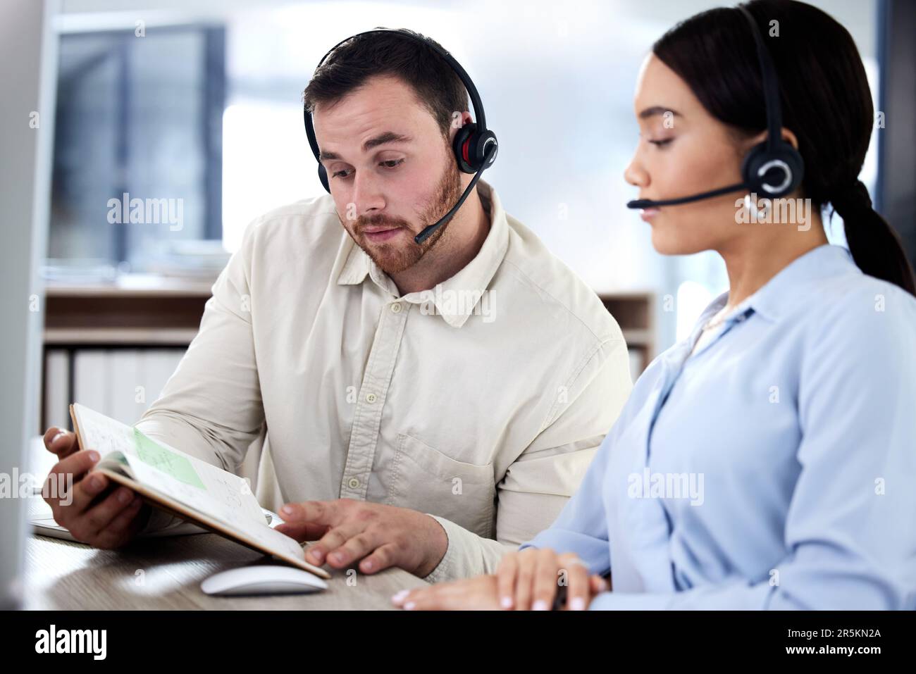 Call center, colleagues reading a notebook and headset at their desk in ...