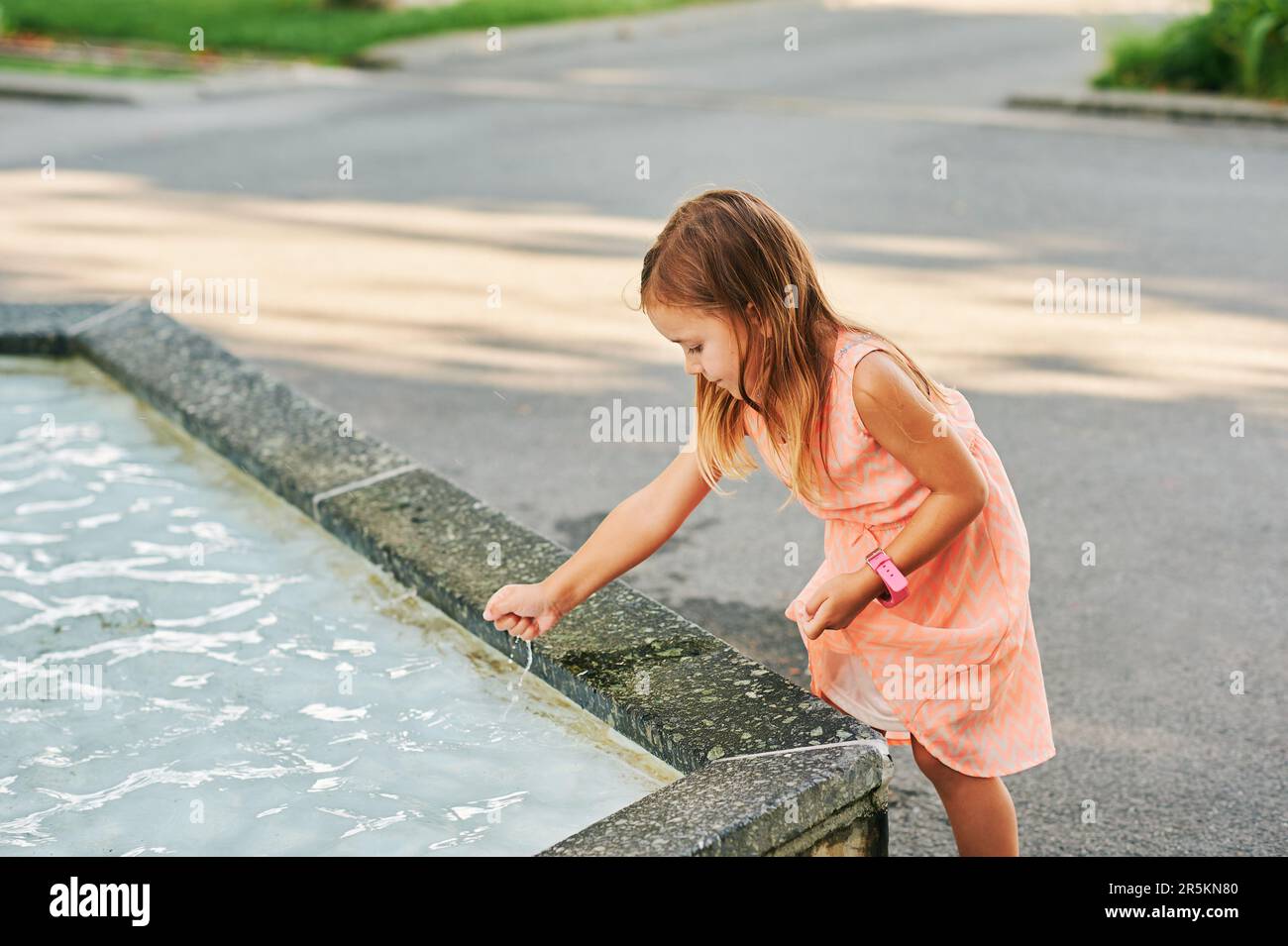 Adorable little girl playing outside, washing dress in water fountain ...
