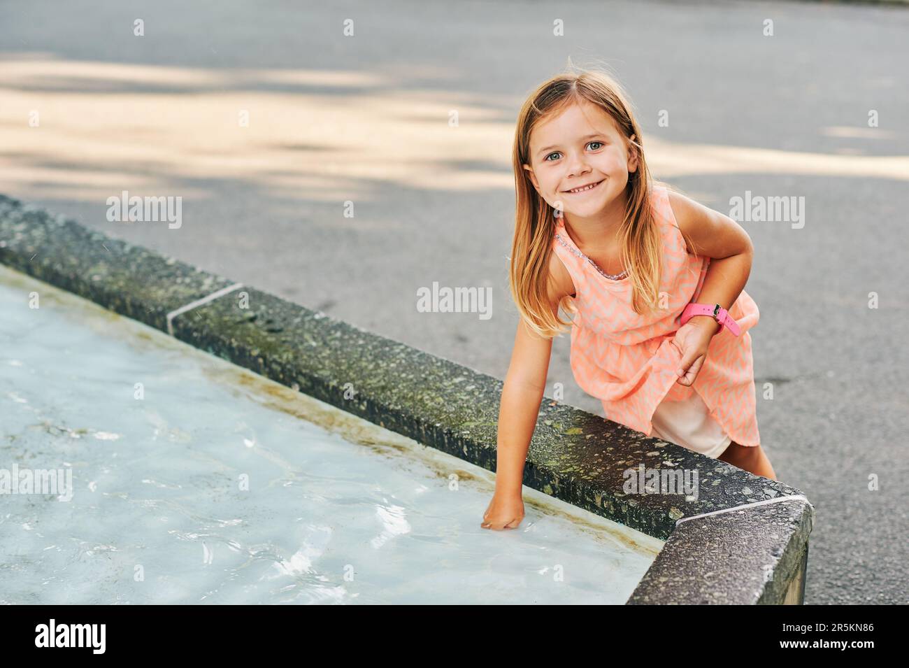 Adorable little girl playing outside, washing dress in water fountain ...