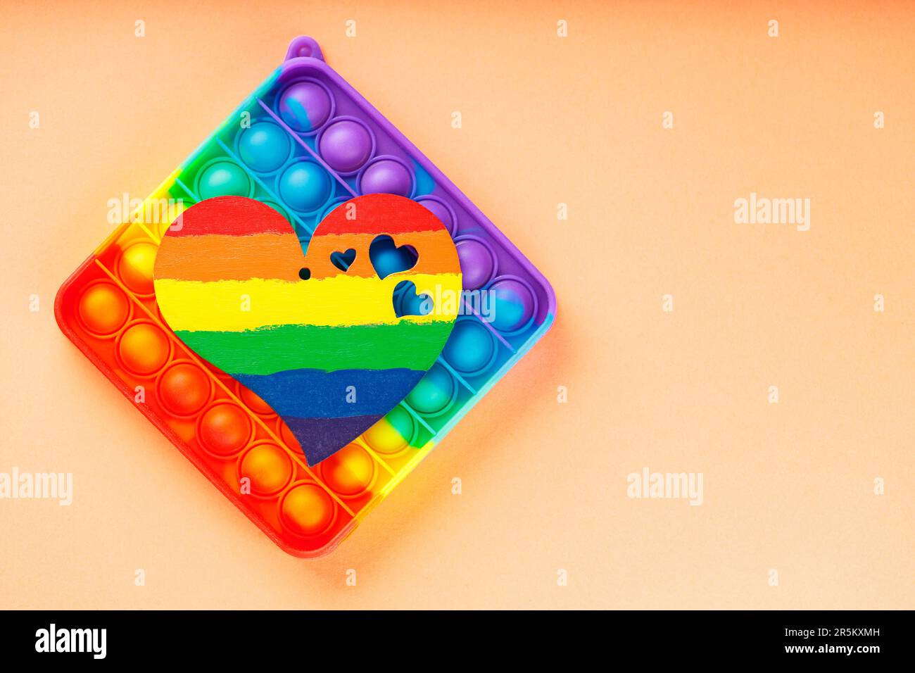 Rainbow heart and multicolored pop it fidget toys on coral background ...