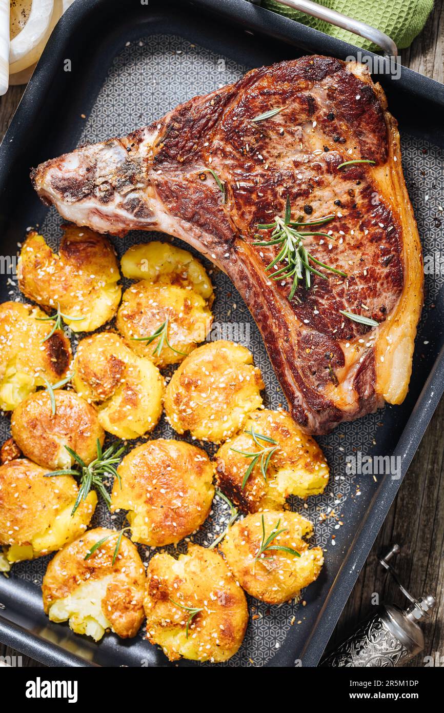 Prime cut of steak with baked potatoes served in metal tray. Seasoned ...