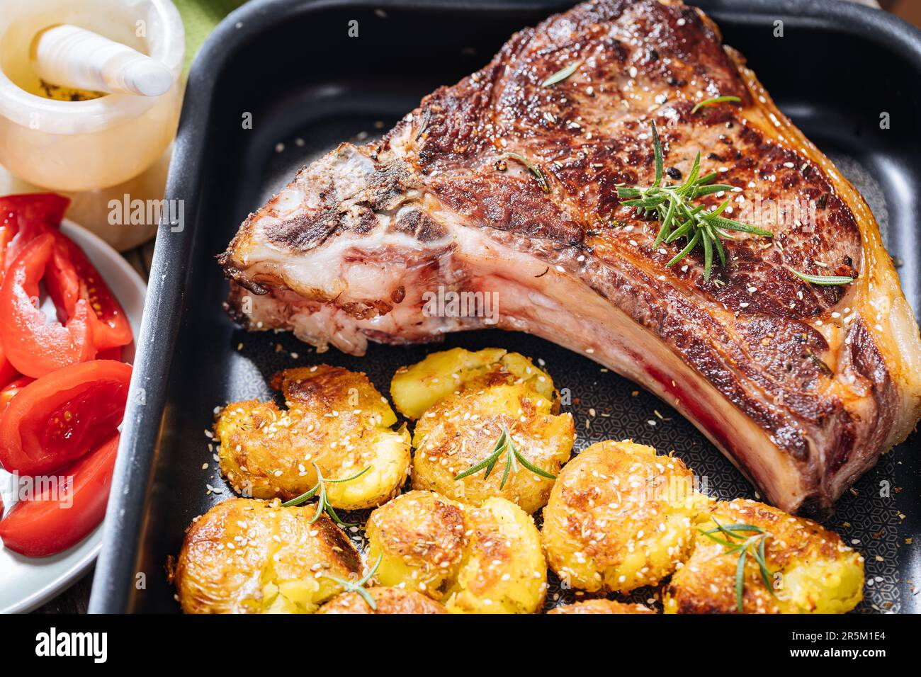 Prime cut of steak with baked potatoes served in metal tray. Seasoned ...