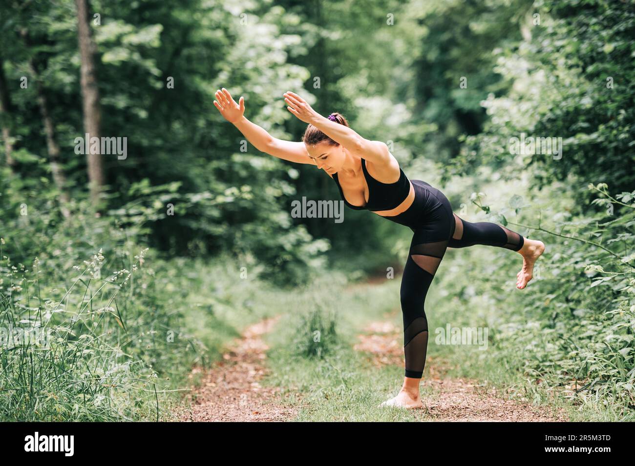 Young fit woman practicing yoga in summer forest, wearing black ...