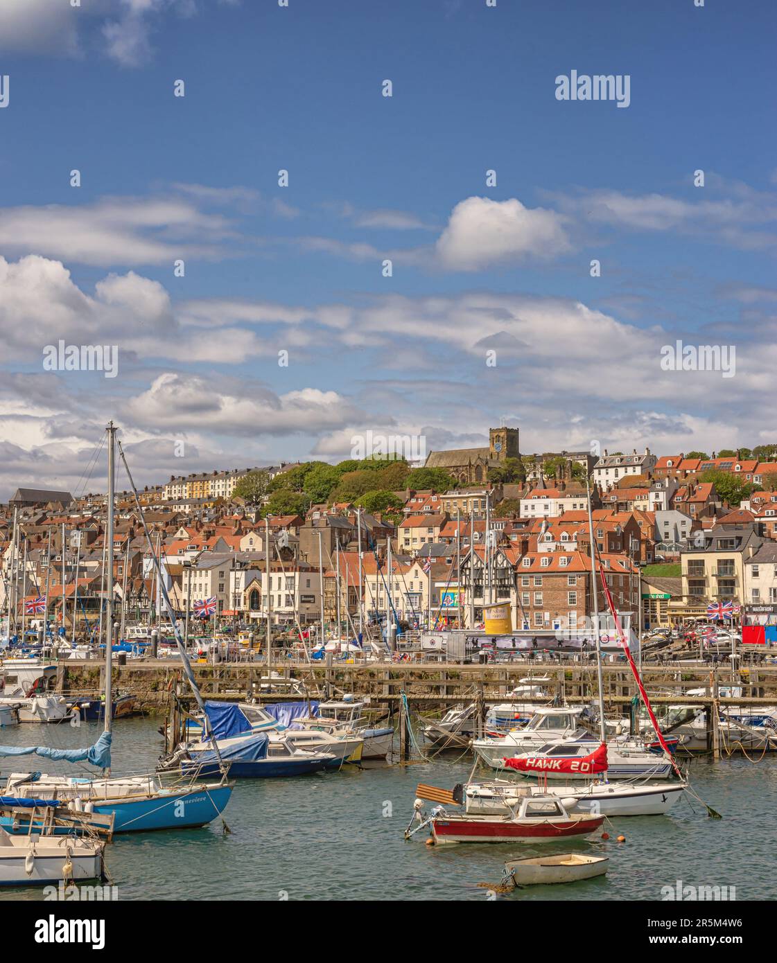 A harbour and marina are in the foreground leading to a seaside town ...