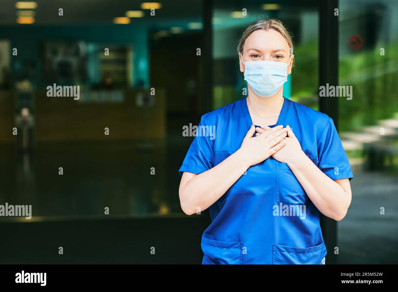 Young female scrub nurse wear blue uniform and face mask, standing in ...