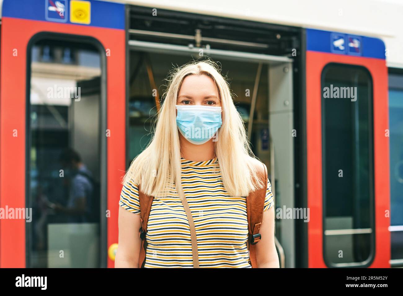 Young woman wearing face mask and backpack, standing at the train station, metro or bus station ...