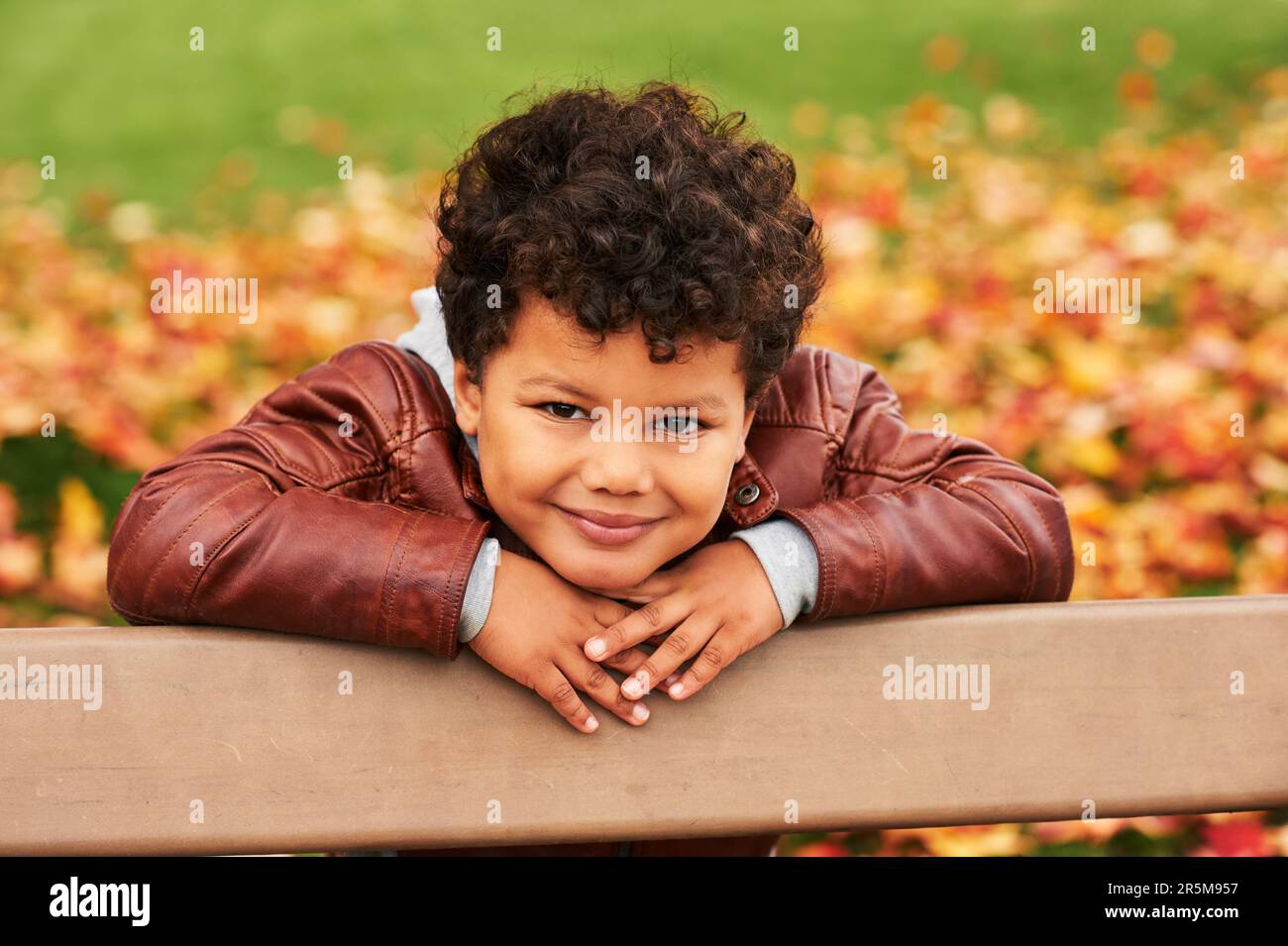 Outdoor close up portrait of adorable little boy leaning on a bench in ...