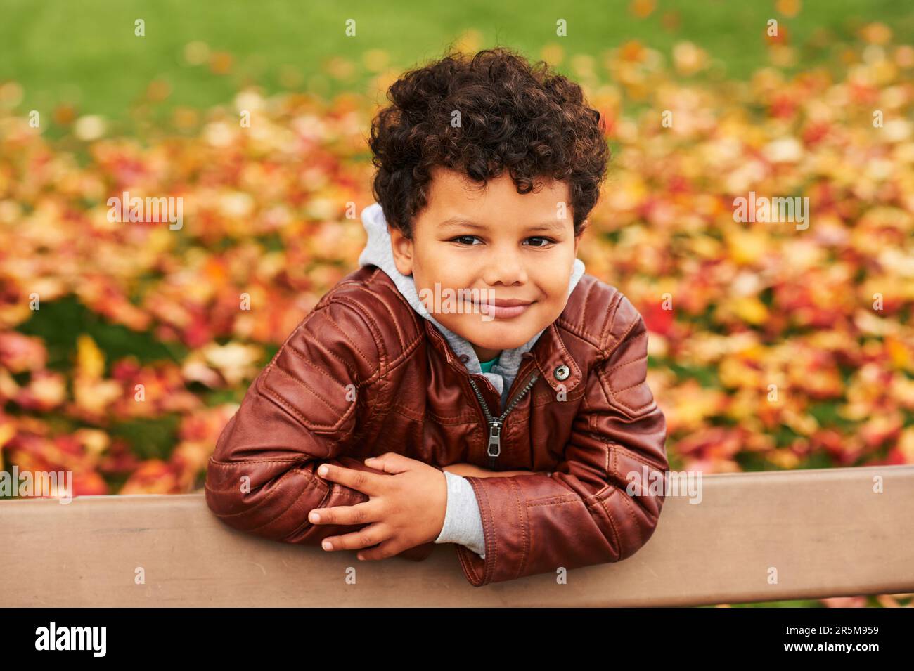 Outdoor close up portrait of adorable little boy leaning on a bench in ...