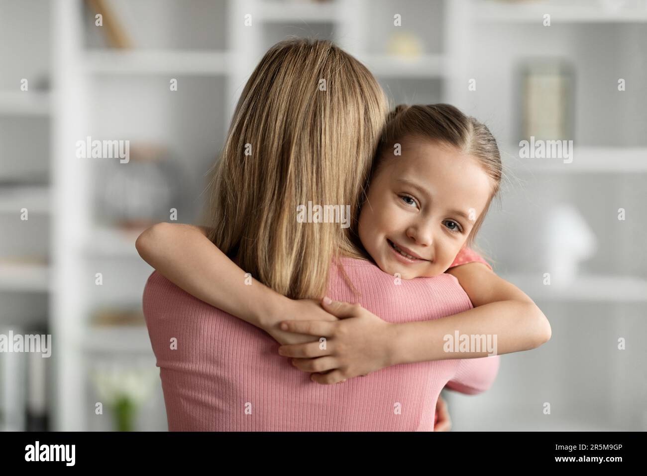 Mother's Day Concept. Cheerful Little Girl Hugging Tight Her Mom At Home Stock Photo - Alamy