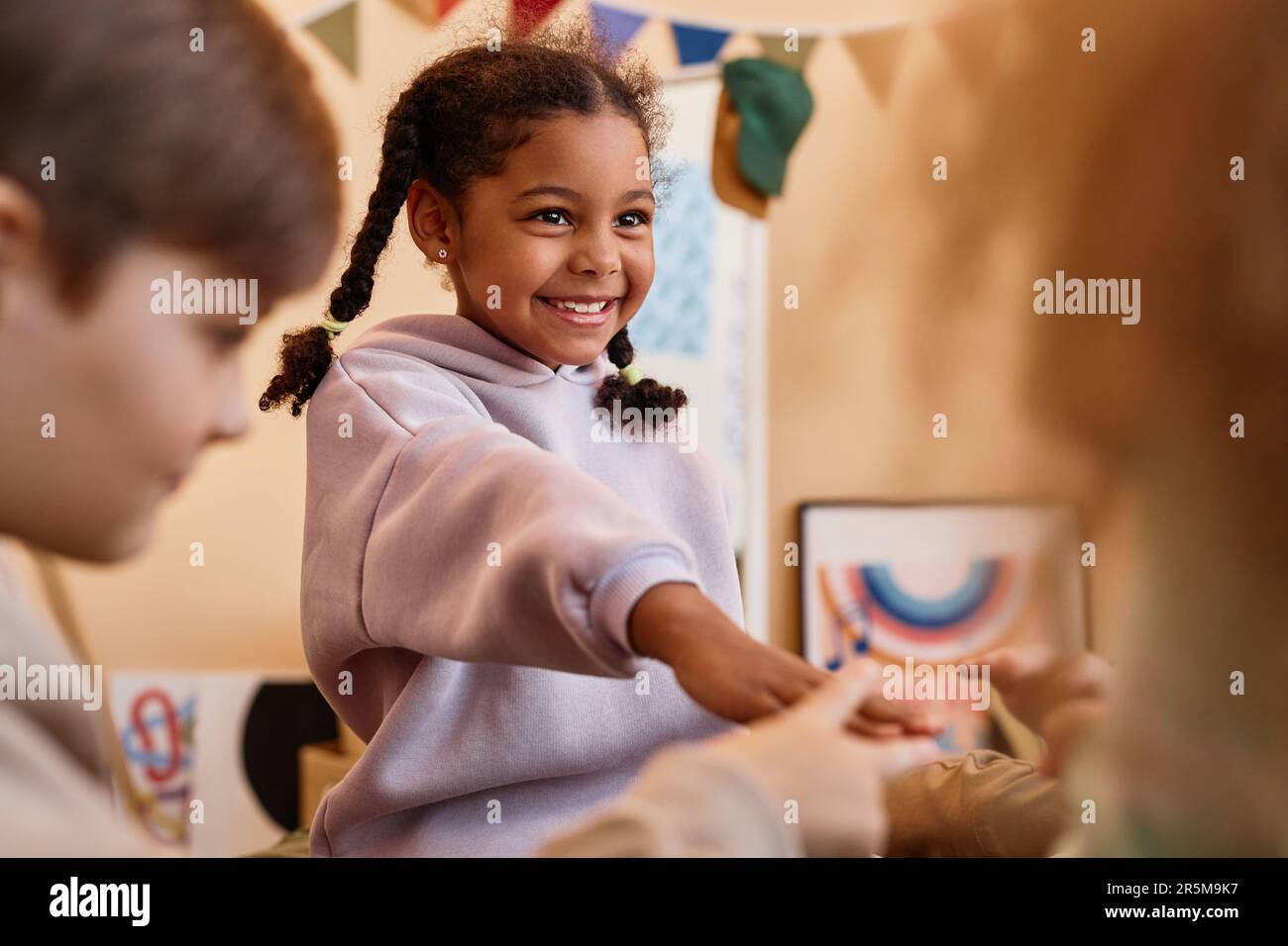 Portrait of cute black girl playing rock paper scissors with friends ...