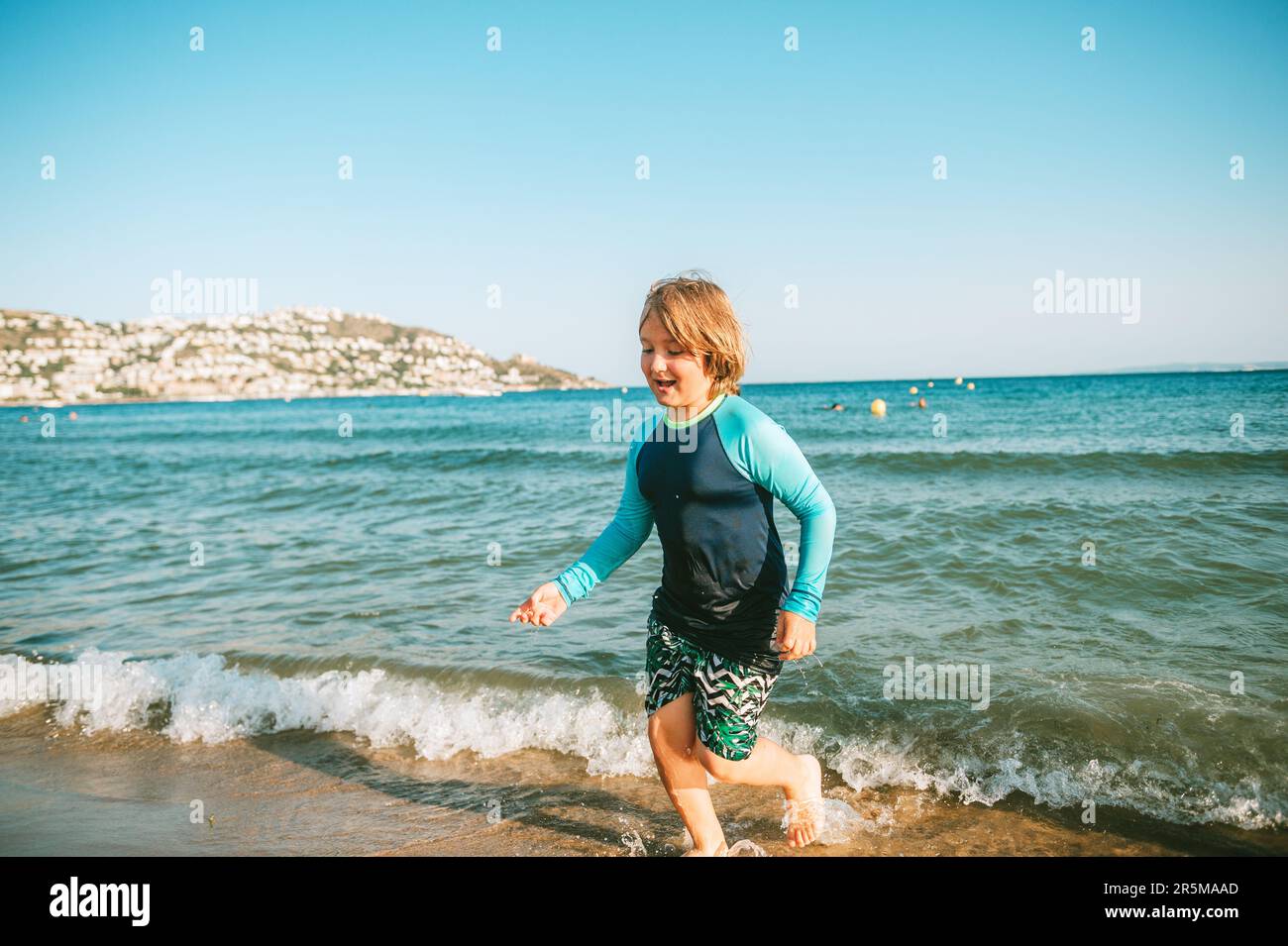 Funny little boy playing by the sea, wearing sun safe rash vest, family ...