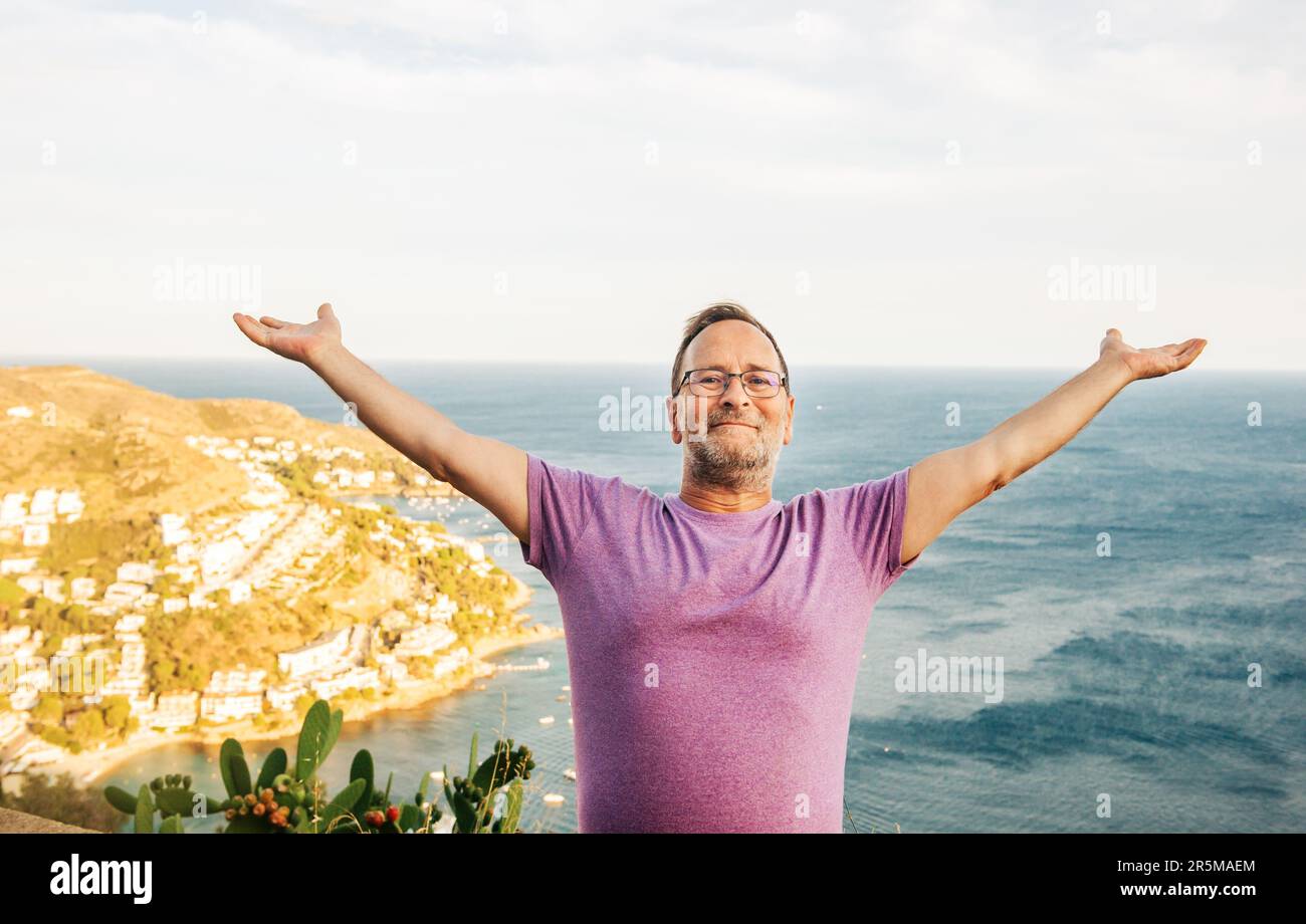 Summer portrait of middle age man posing by the sea, arms wide open ...