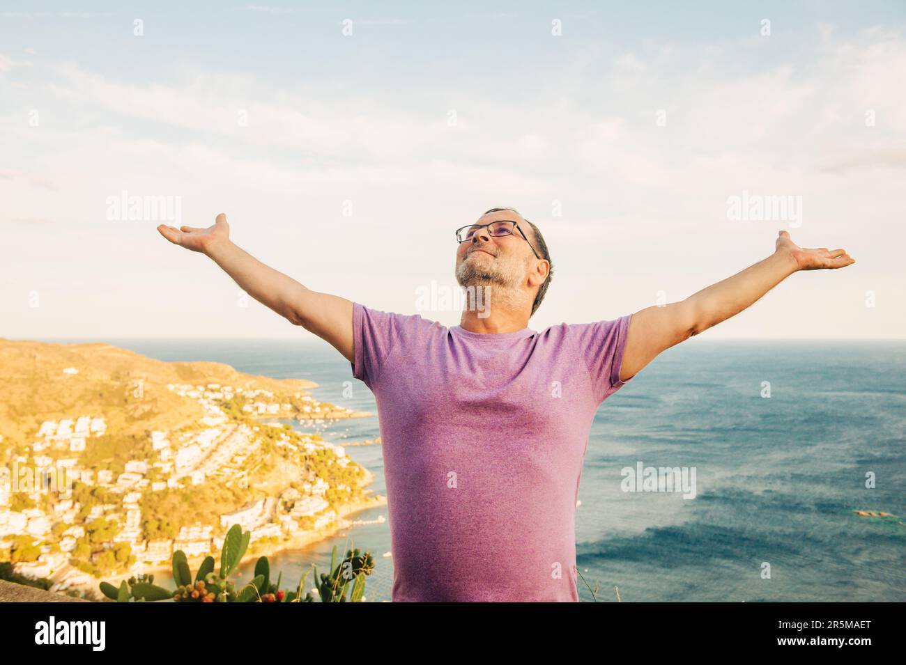 Summer portrait of middle age man posing by the sea, arms wide open ...