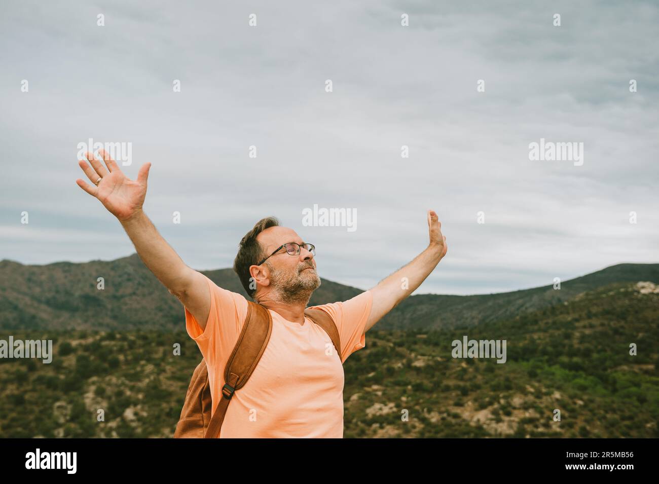 Man standing on the top of the hill, wearing backpack, arms wide open ...