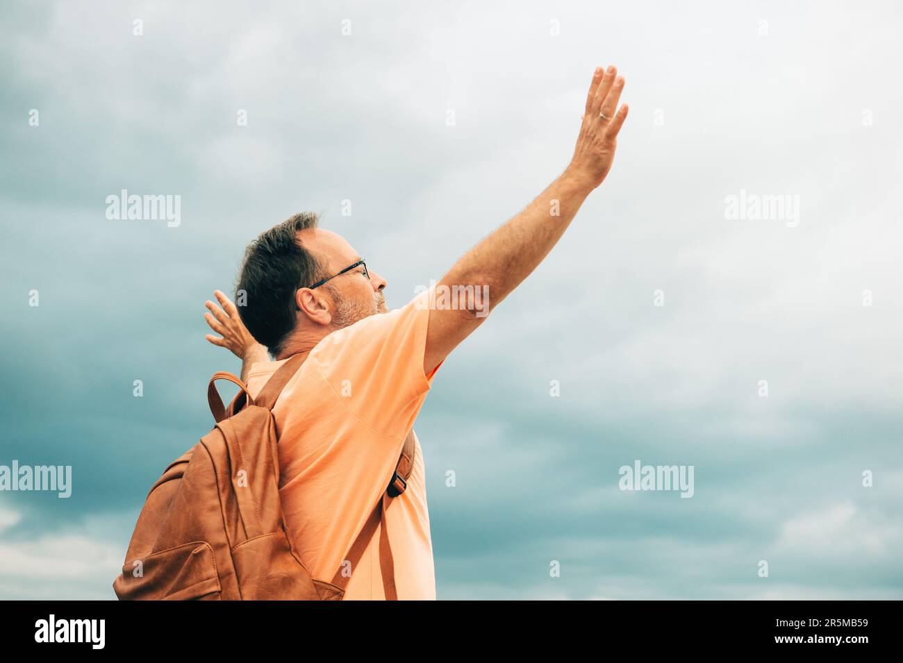Man standing on the top of the hill, wearing backpack, arms wide open ...