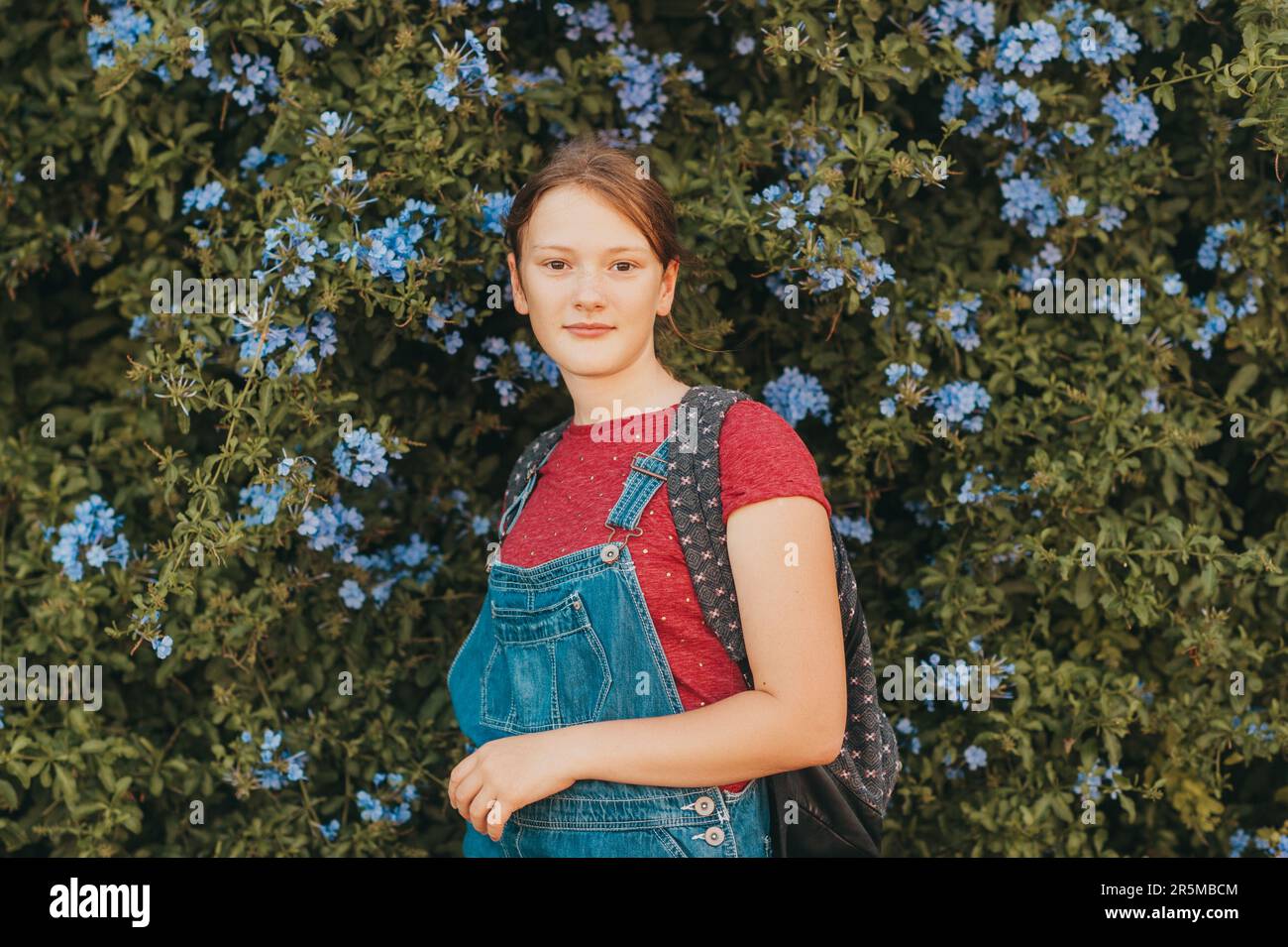 Outdoor portrait of pretty teenage girl, wearing overalls and backpack ...