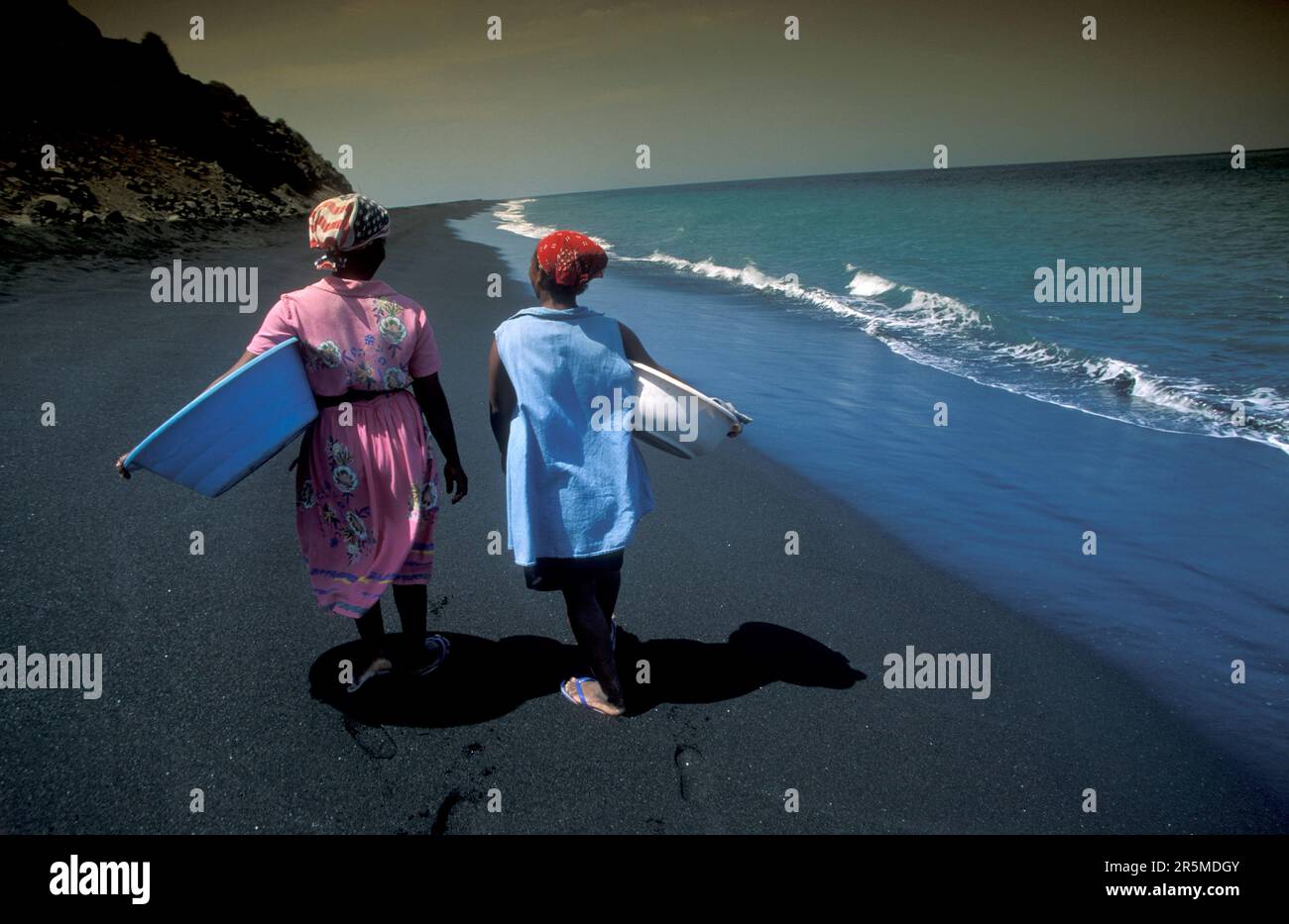 two women at the black sand beach of volcanic lava sand at the town of ...