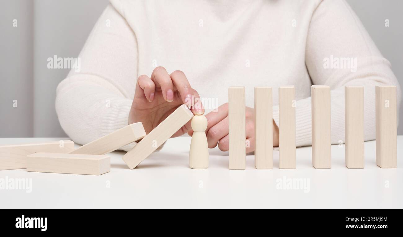 Hand stops the fall of wooden figurines of men on a white background ...