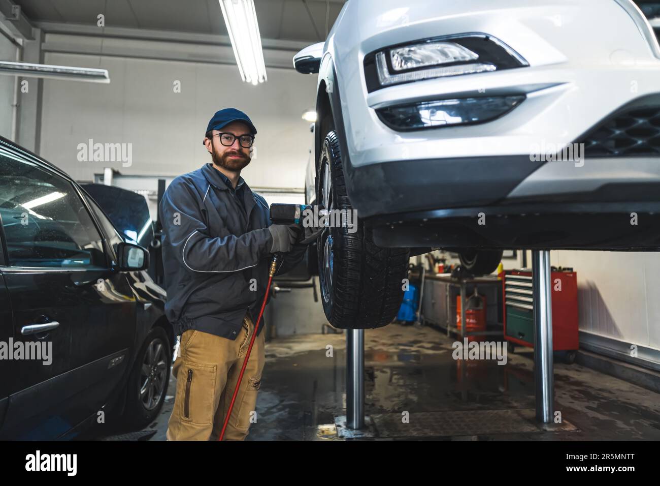 Auto mechanic standing by the car on a lift and replacing a wheel with ...