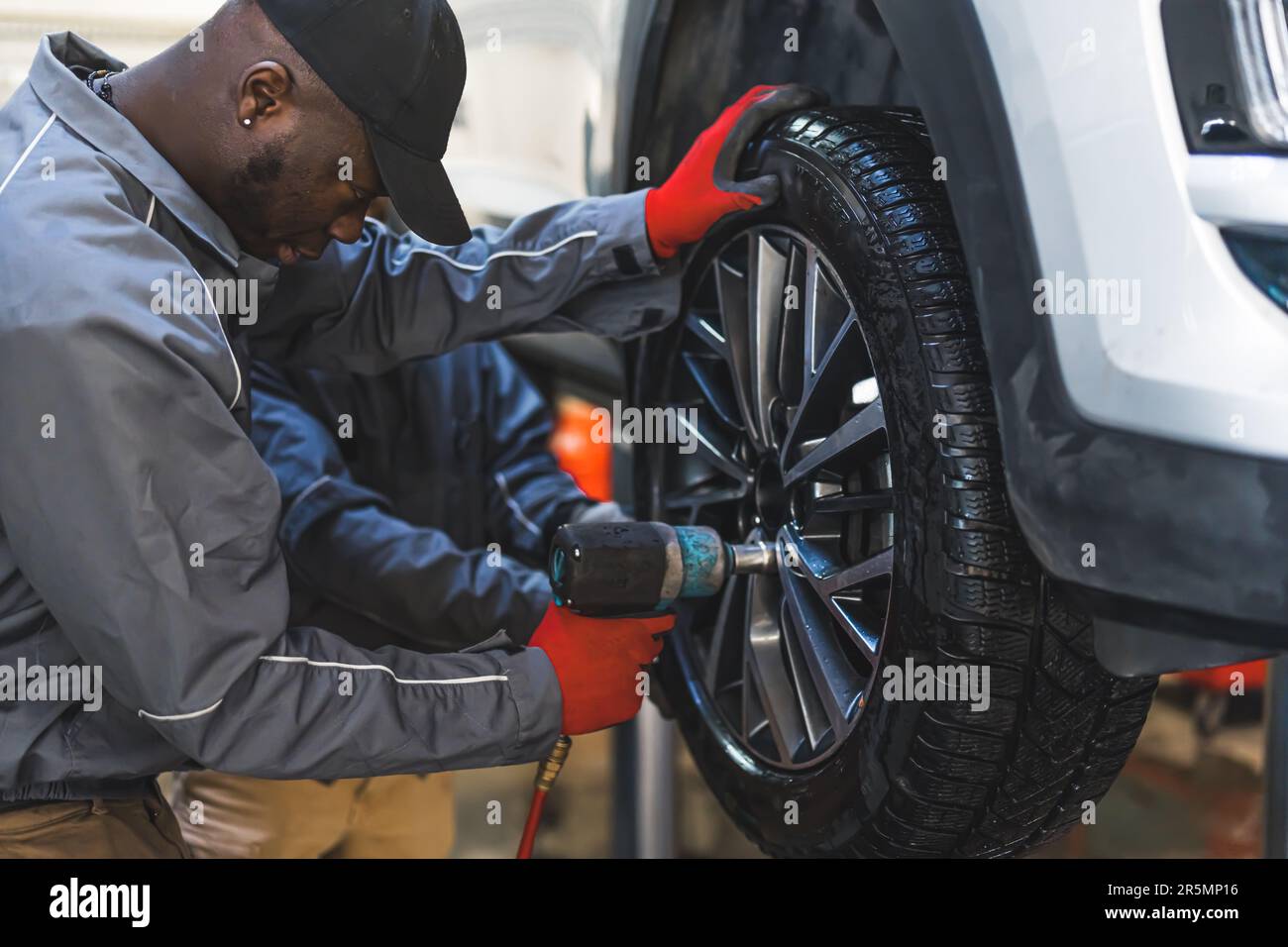 Two men auto mechanics changing car tire on a vehicle on a hoist using ...