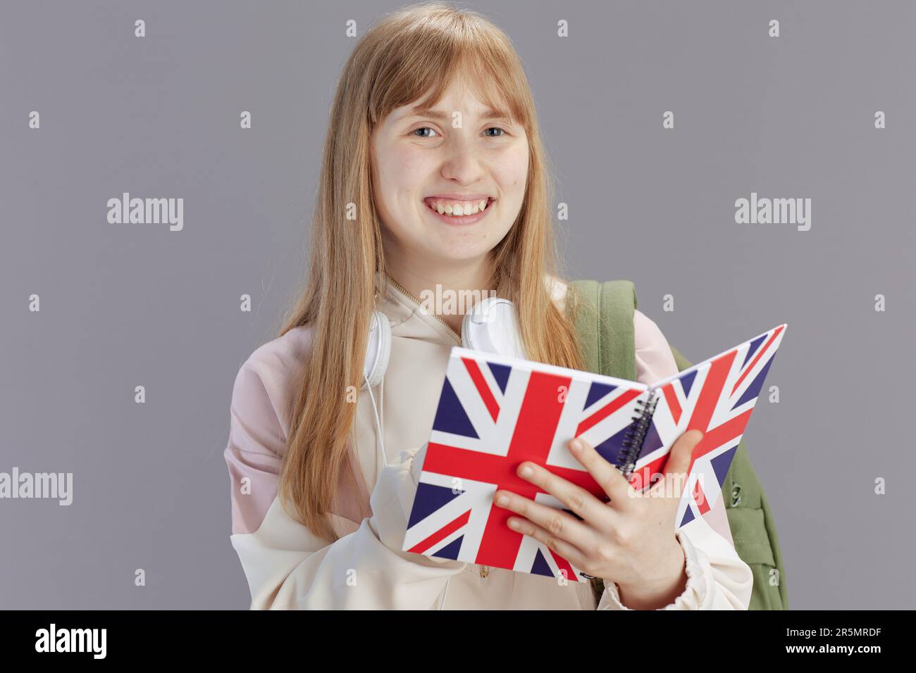 smiling modern teenager girl in beige tracksuit with backpack, english ...