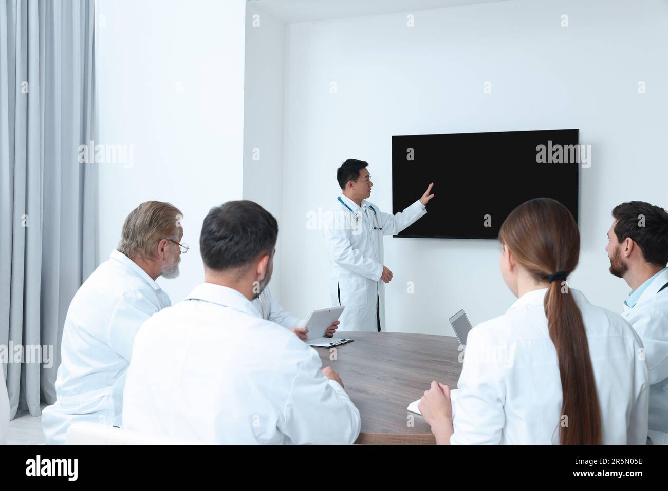 Team of doctors listening to speaker report near tv screen in meeting ...