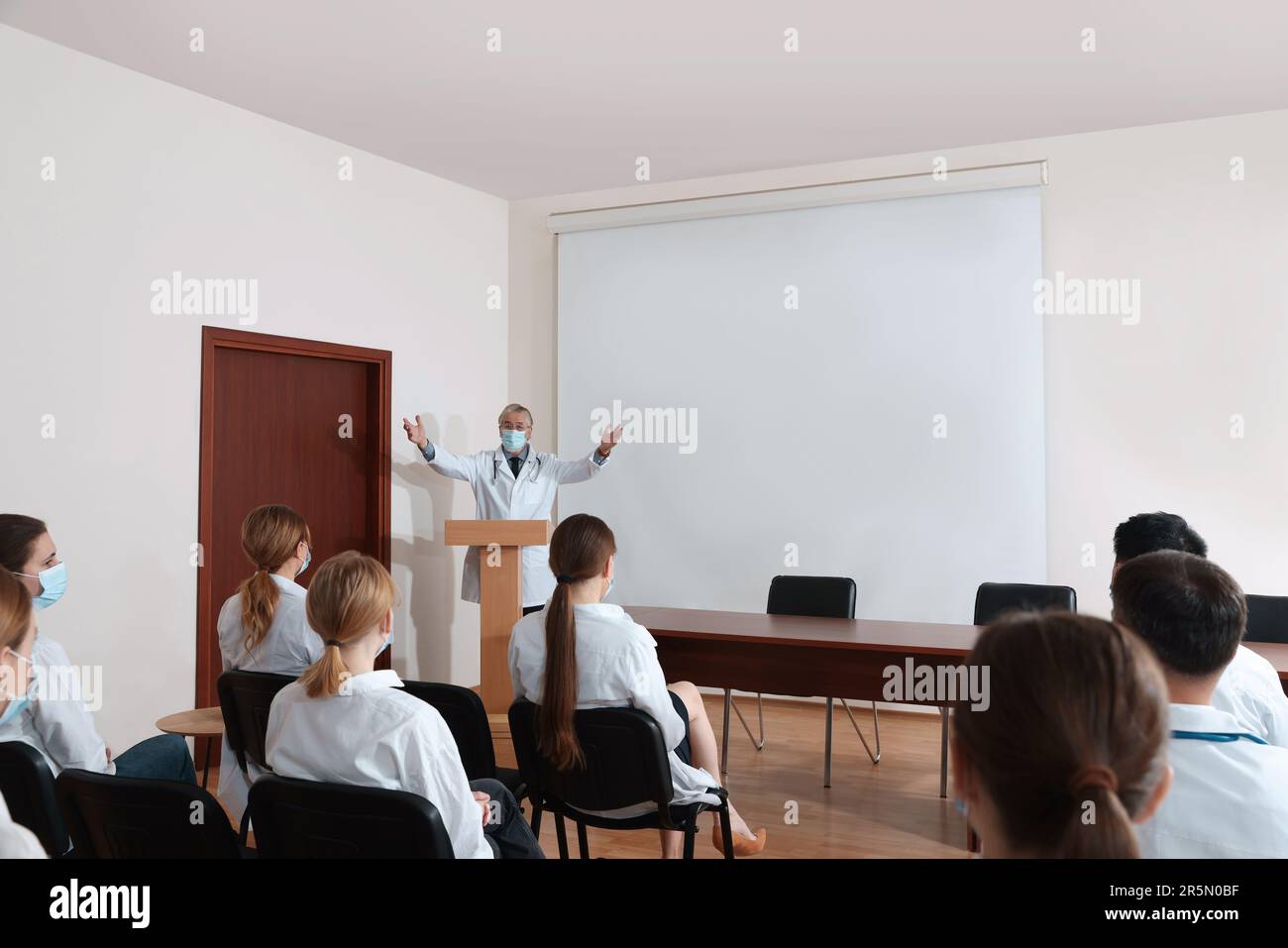Senior doctor giving lecture near projection screen in conference room ...