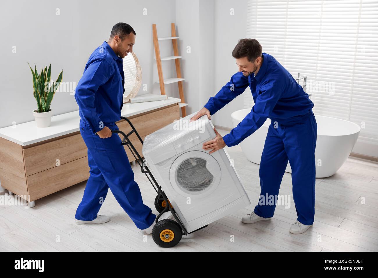 Male movers carrying washing machine in bathroom. New house Stock Photo ...