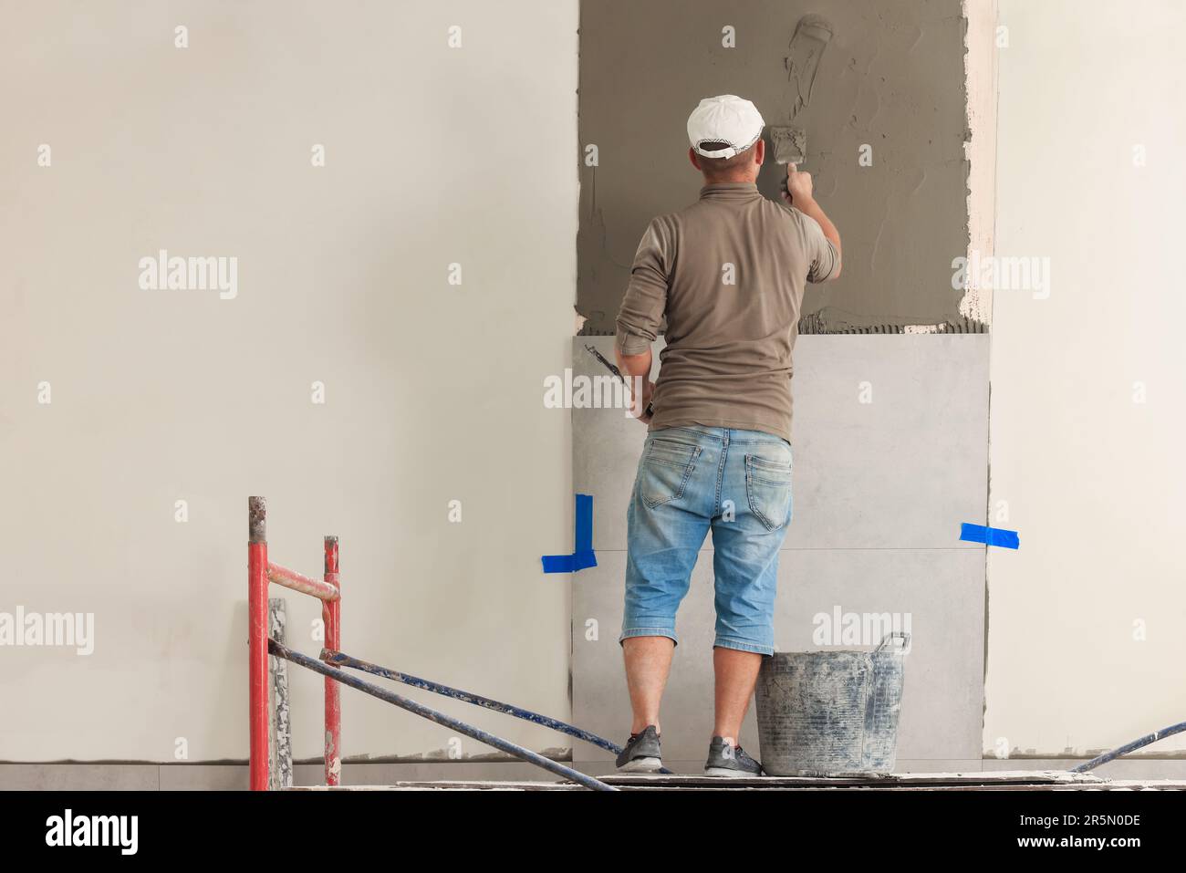 Worker spreading adhesive mix over wall for tile installation indoors ...