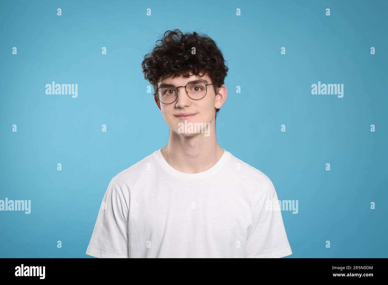 Portrait of cute teenage boy wearing glasses on light blue background ...