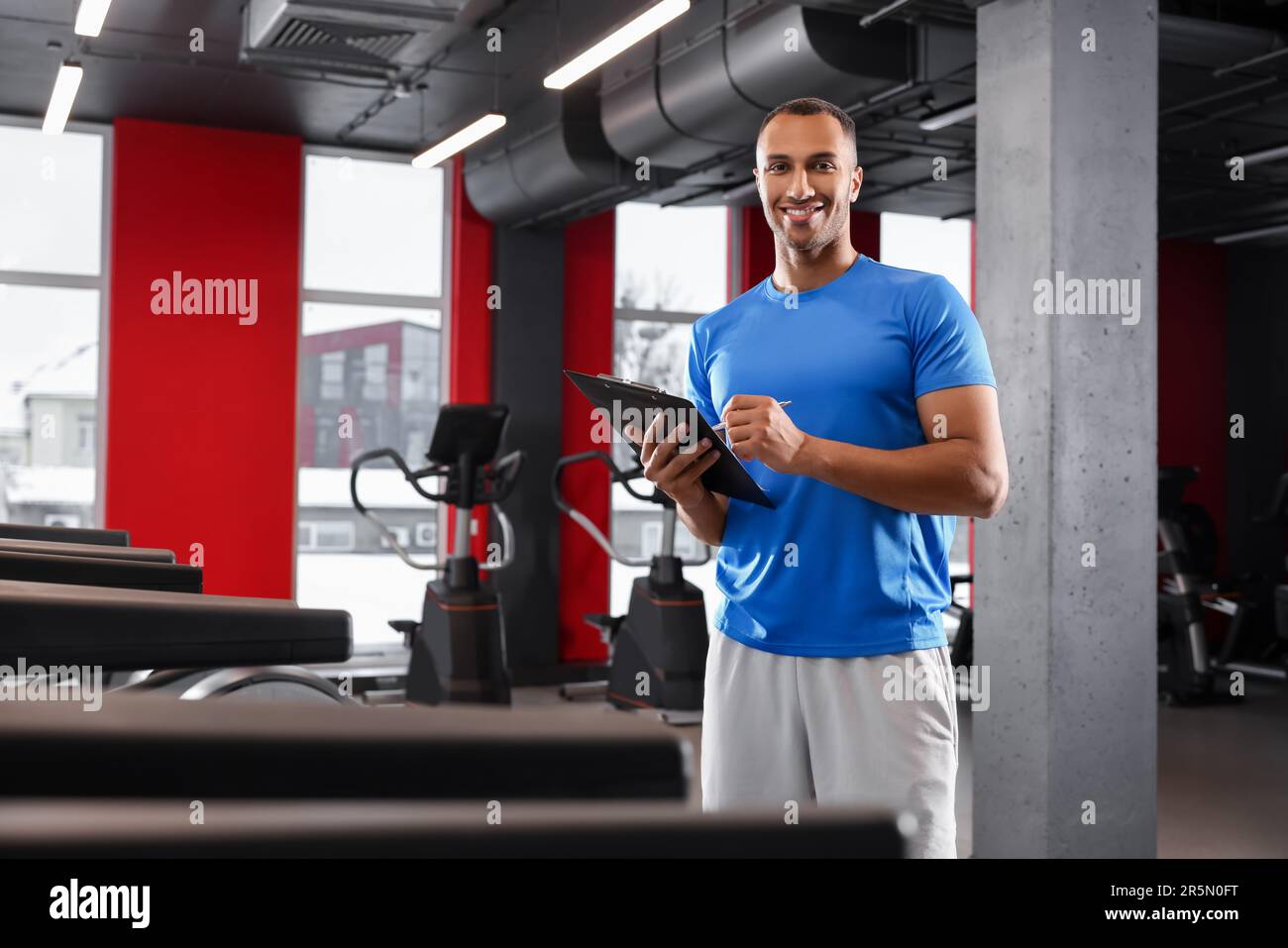 Happy trainer writing down workout plan in modern gym, space for text ...