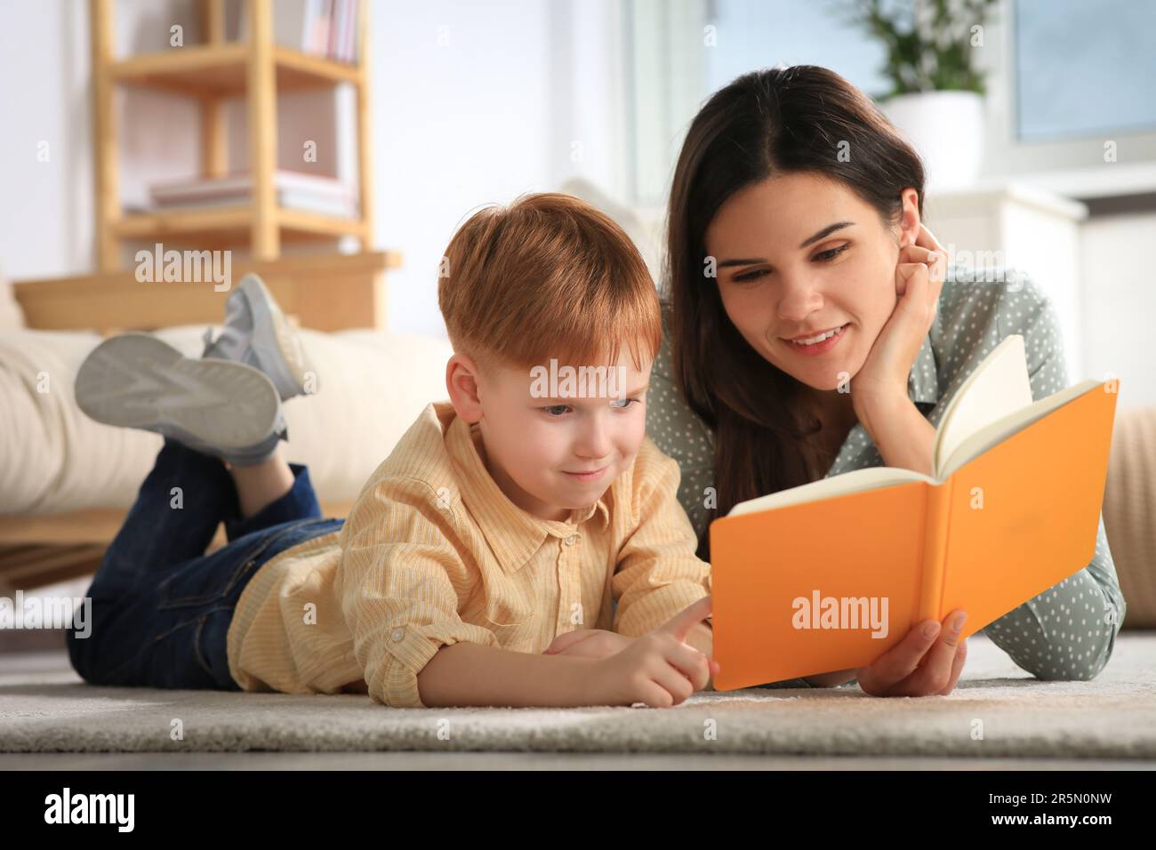 Mother reading book with her son on floor in living room at home Stock ...