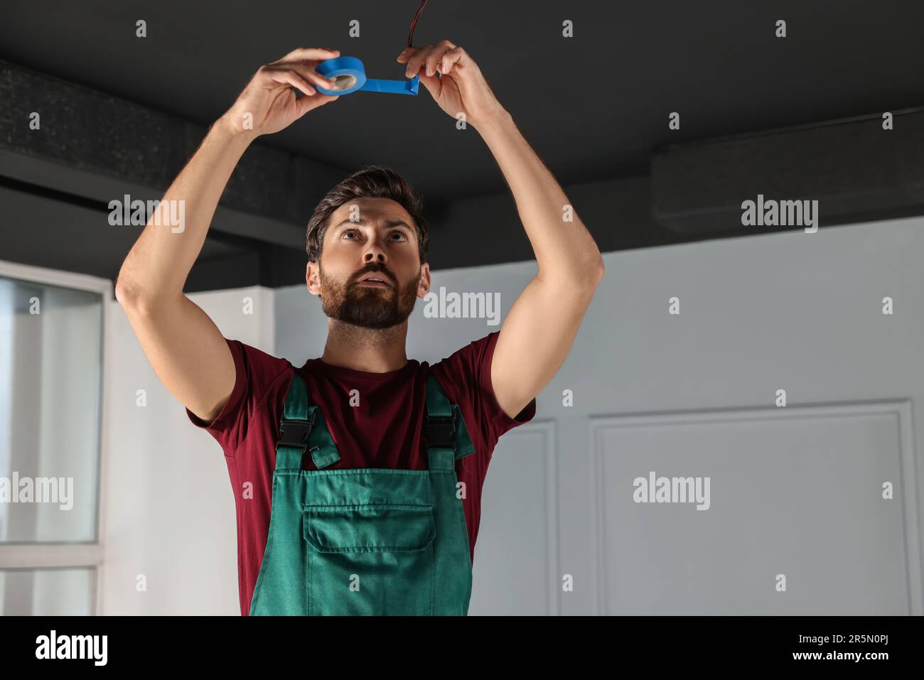 Electrician repairing ceiling wiring with insulting tape indoors Stock ...