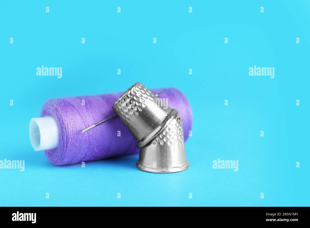Thimbles and spool of purple sewing thread with needle on light blue ...