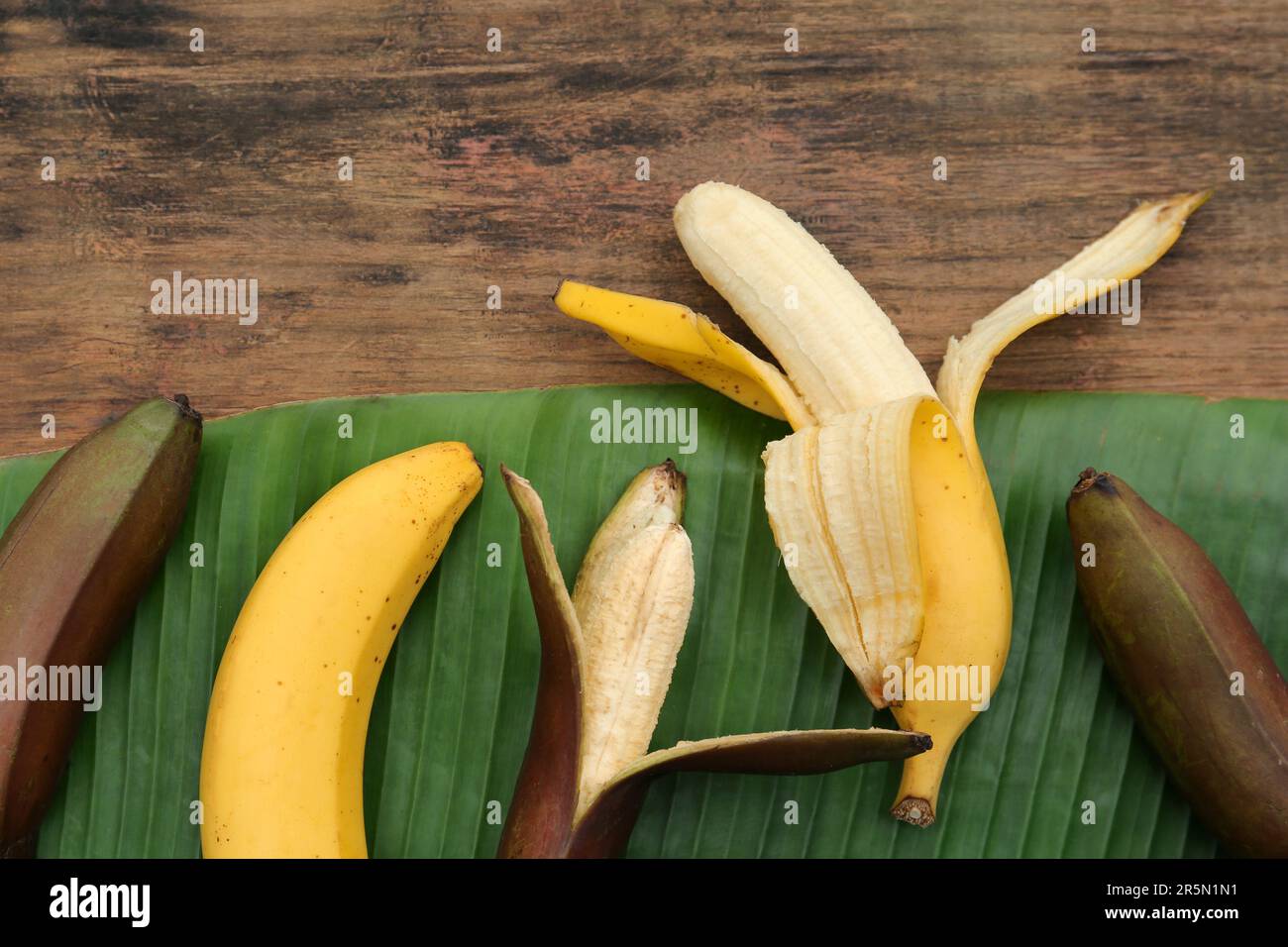 Different types of bananas and fresh leaf on wooden table, flat lay ...