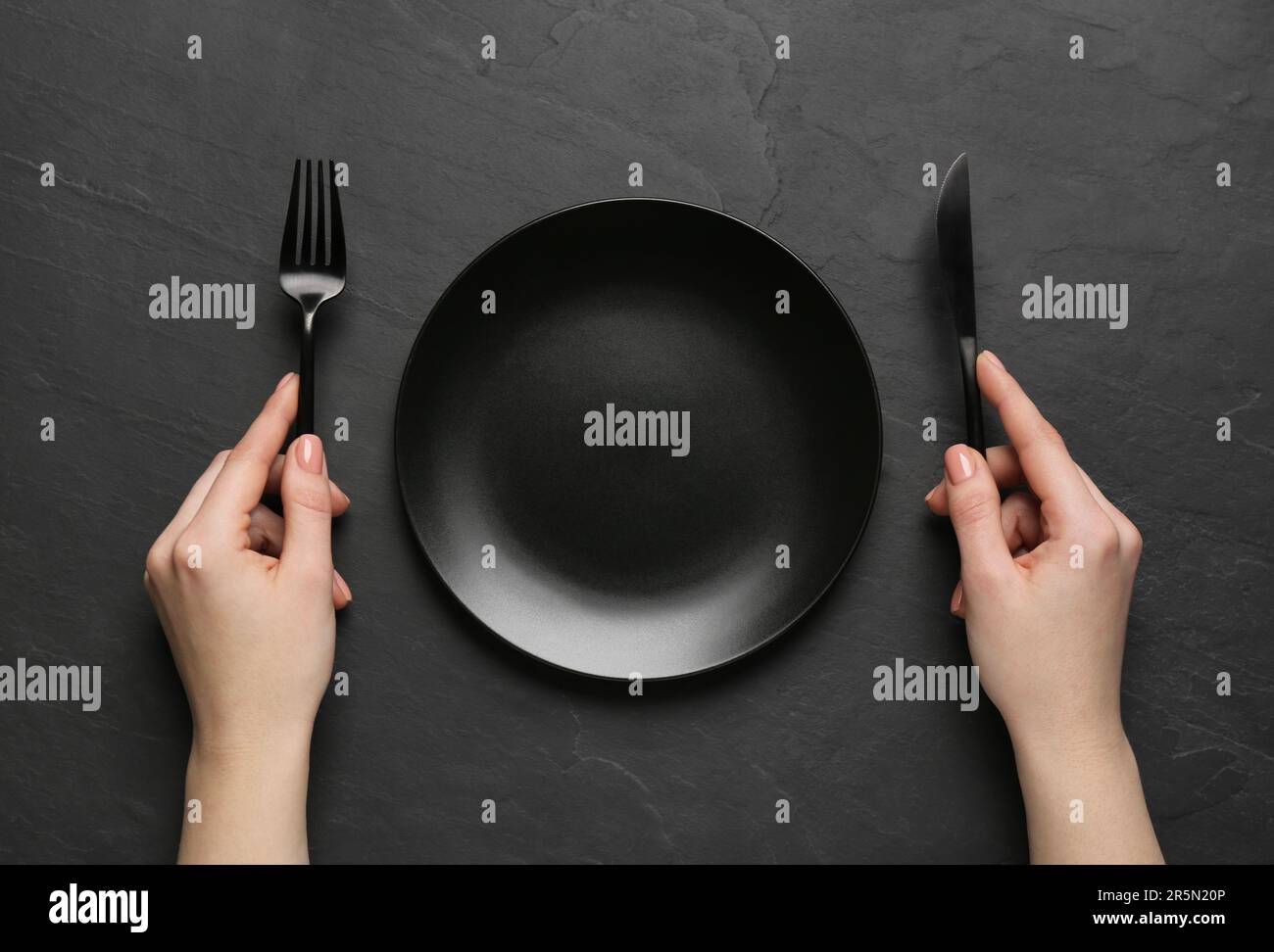 Woman with empty plate and cutlery at black table, top view Stock Photo ...