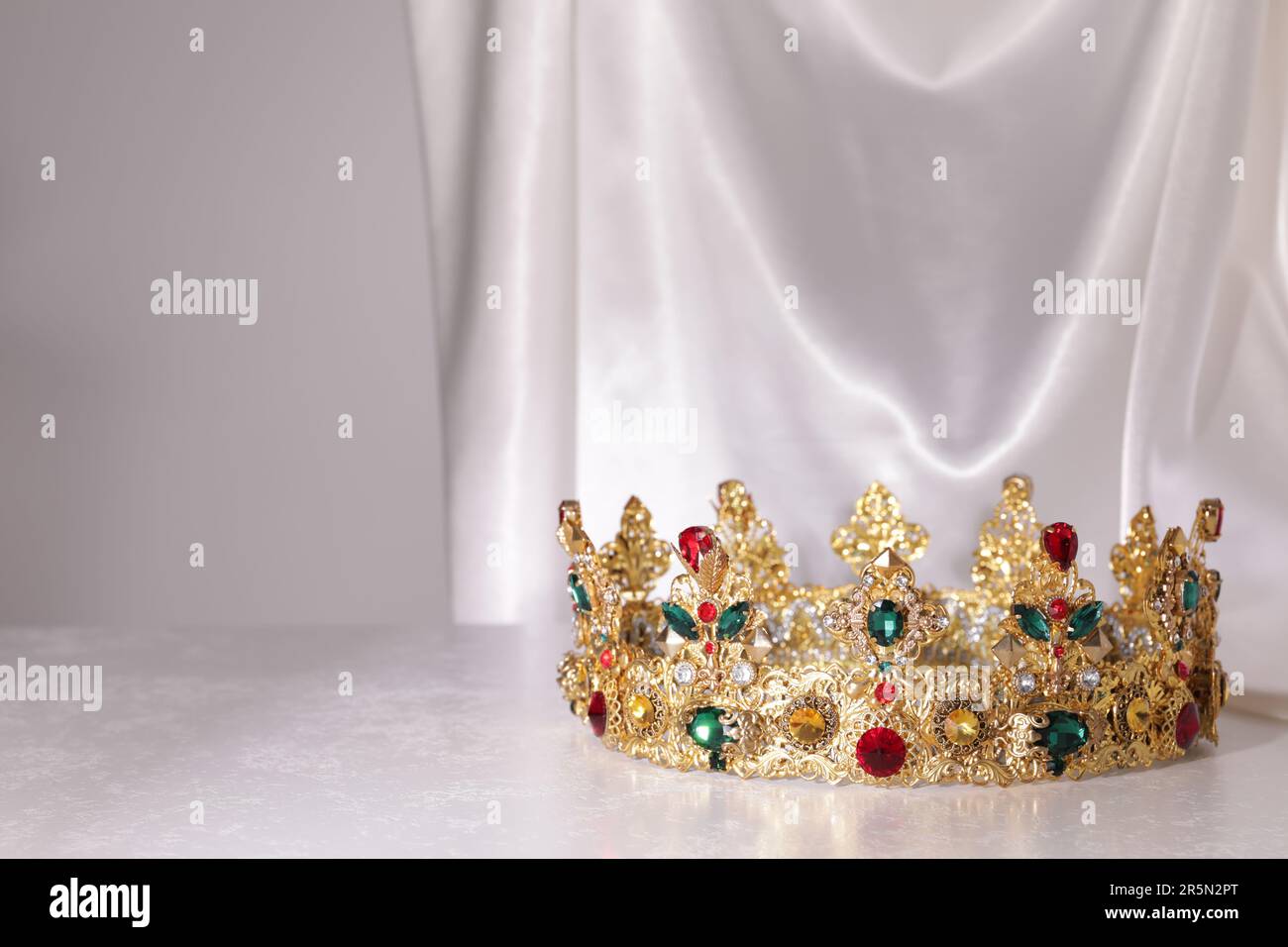 Beautiful golden crown with gems on light grey table. Space for text ...