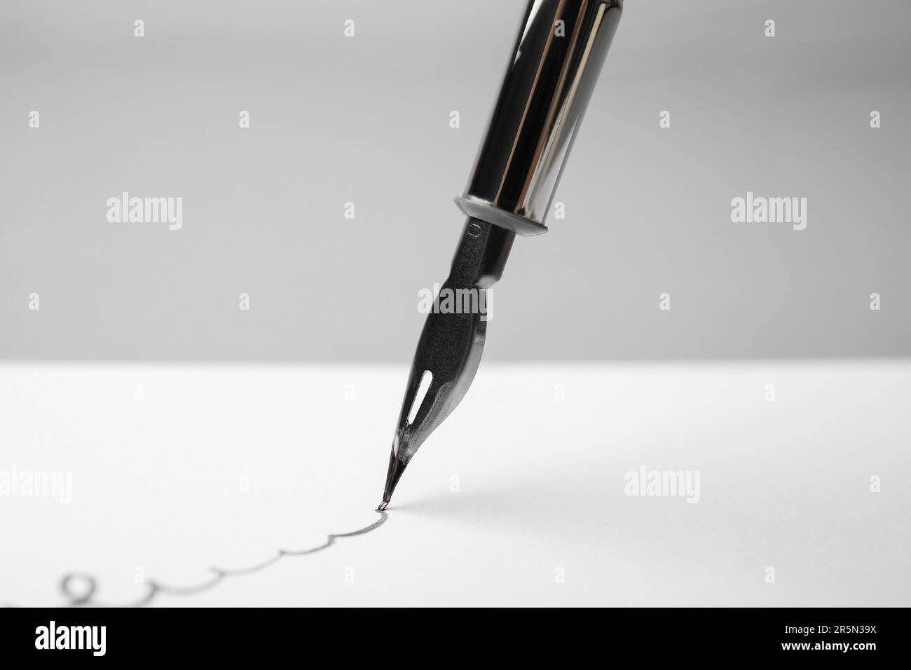 Signing on sheet of paper with fountain pen against light grey ...