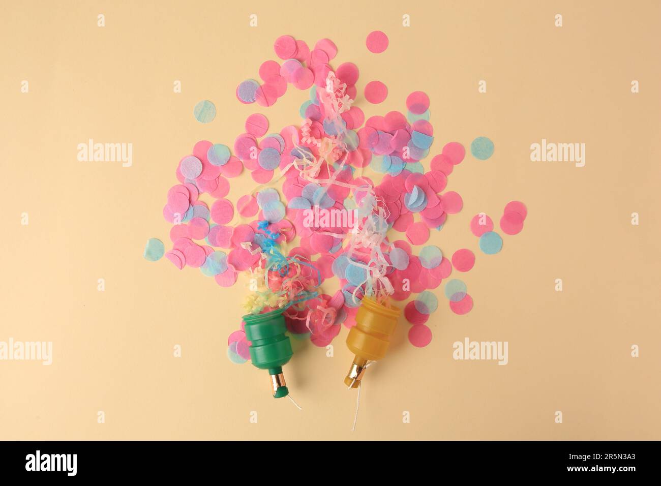 Colorful confetti and serpentine bursting out of party poppers on beige ...