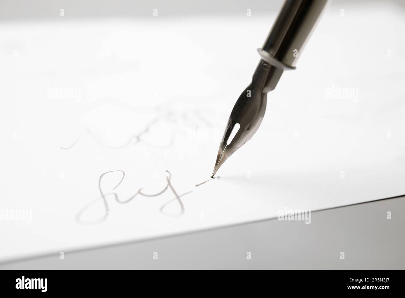 Signing on sheet of paper with fountain pen against light grey ...