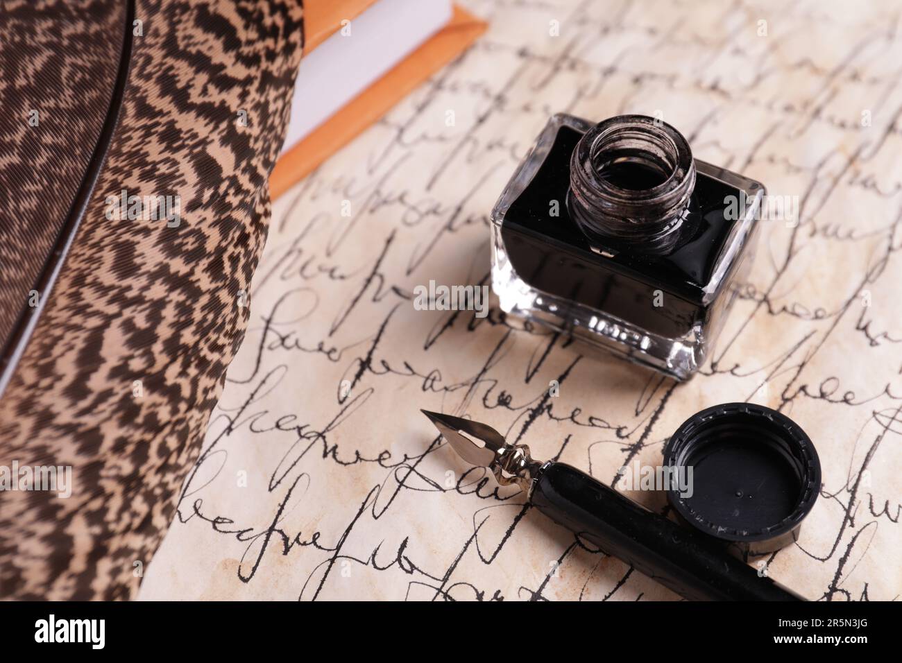 Open inkwell, fountain pen, feather and book on vintage parchment with ...