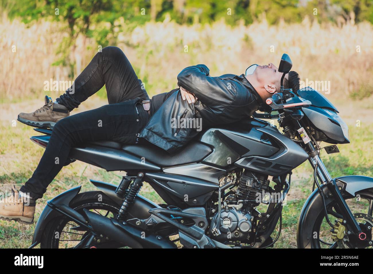 Motorcyclist in jacket lying on his motorcycle in the countryside ...