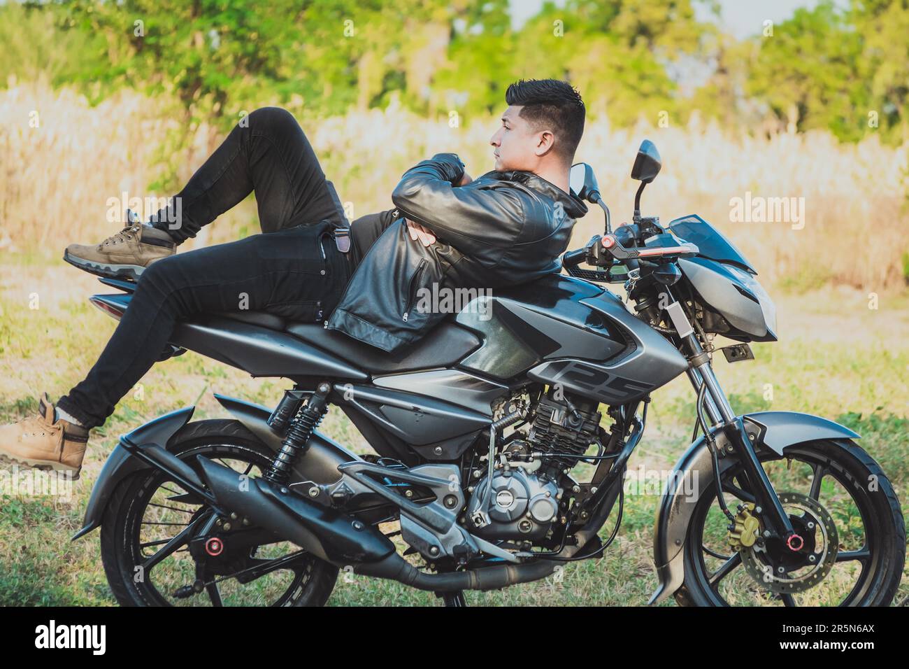 Biker man lying down on his motorbike outdoors. Motorcyclist in jacket ...