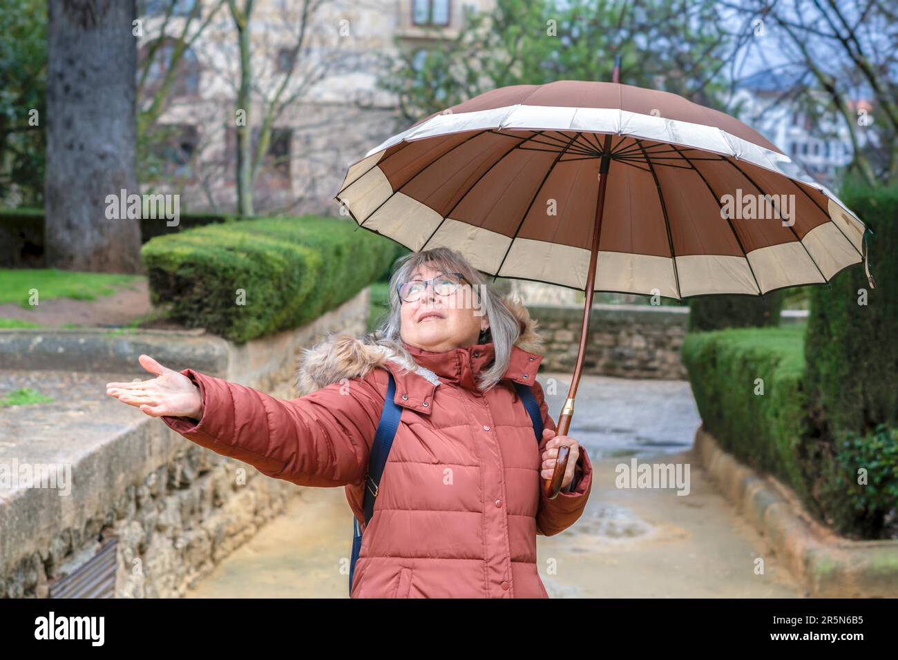 Elderly woman with umbrella on a rainy day holding out her hand to see ...