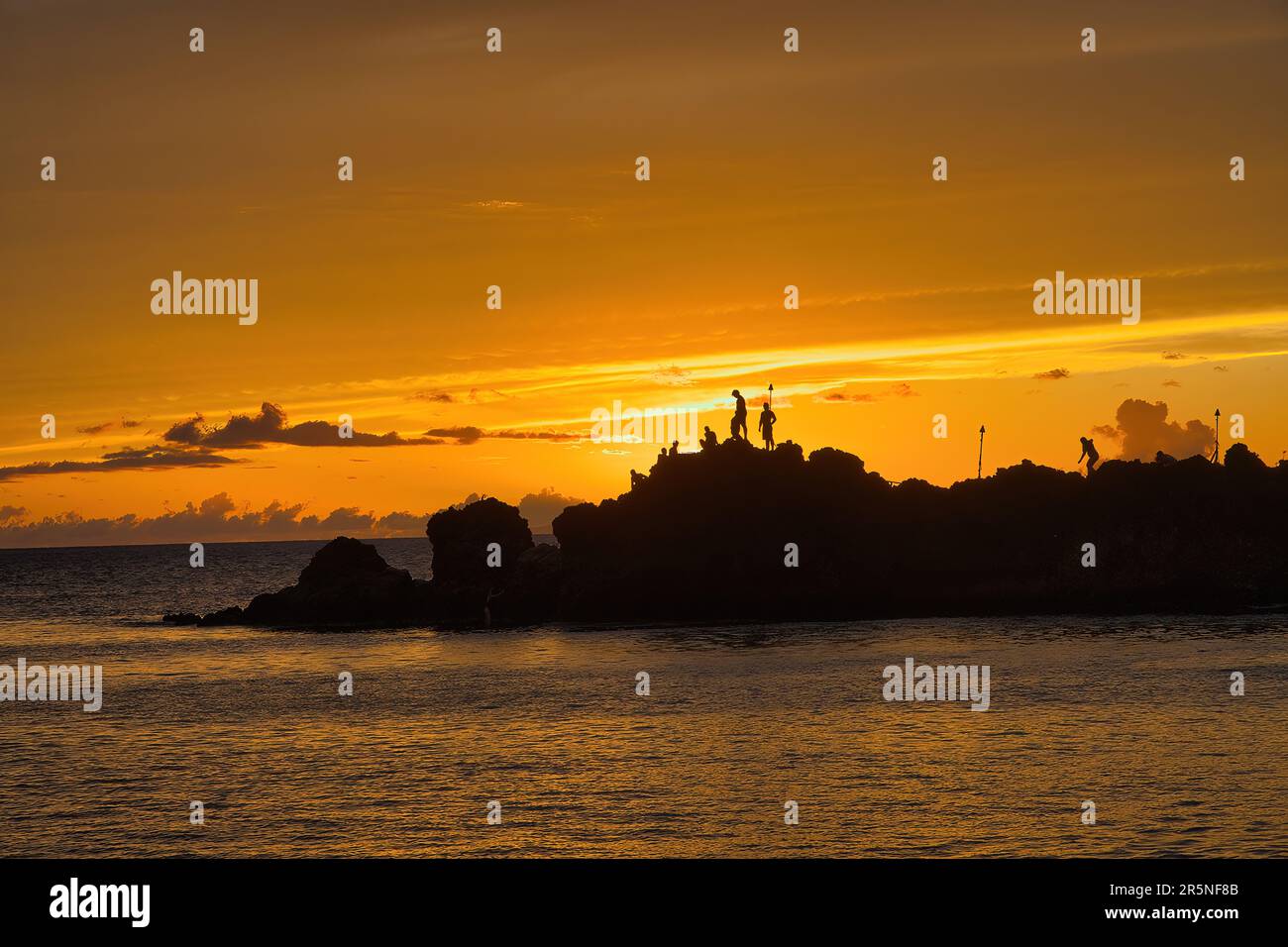 Silhouetted cliff divers preparing to dive at sunset at Black Rock on ...