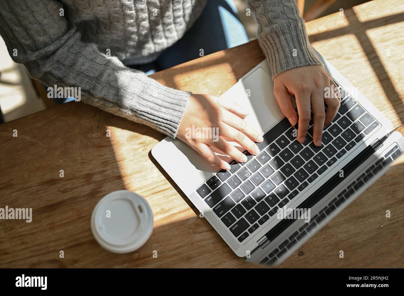 Top view of a female in a grey sweater typing on a laptop keyboard ...